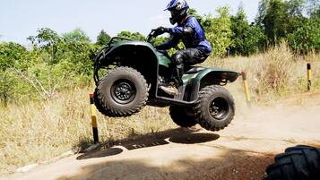 Uma pessoa conduz uma moto de trilha por um caminho de terra, rodeada por vegetação.