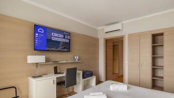 Quarto de hotel com uma cama, escrivaninha, cadeira, televisão fixada na parede e guarda-roupa.