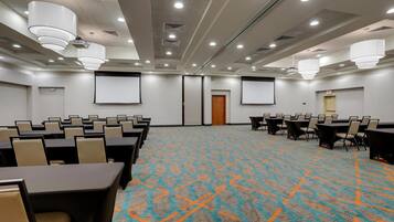 Sala de conferências com carpete estampado, várias mesas, cadeiras e um projetor.