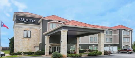 Um hotel La Quinta com fachada de pedra, entrada coberta e telhado de telhas vermelhas.
