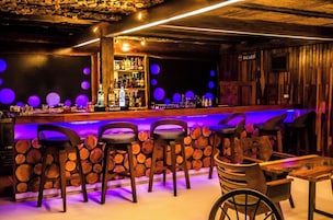 Uma área de bar com bancos de madeira, balcão e uma pilha de lenha atrás do balcão.