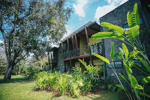 Um edifício de dois andares com fachada de pedra, cercado por vegetação exuberante e árvores.