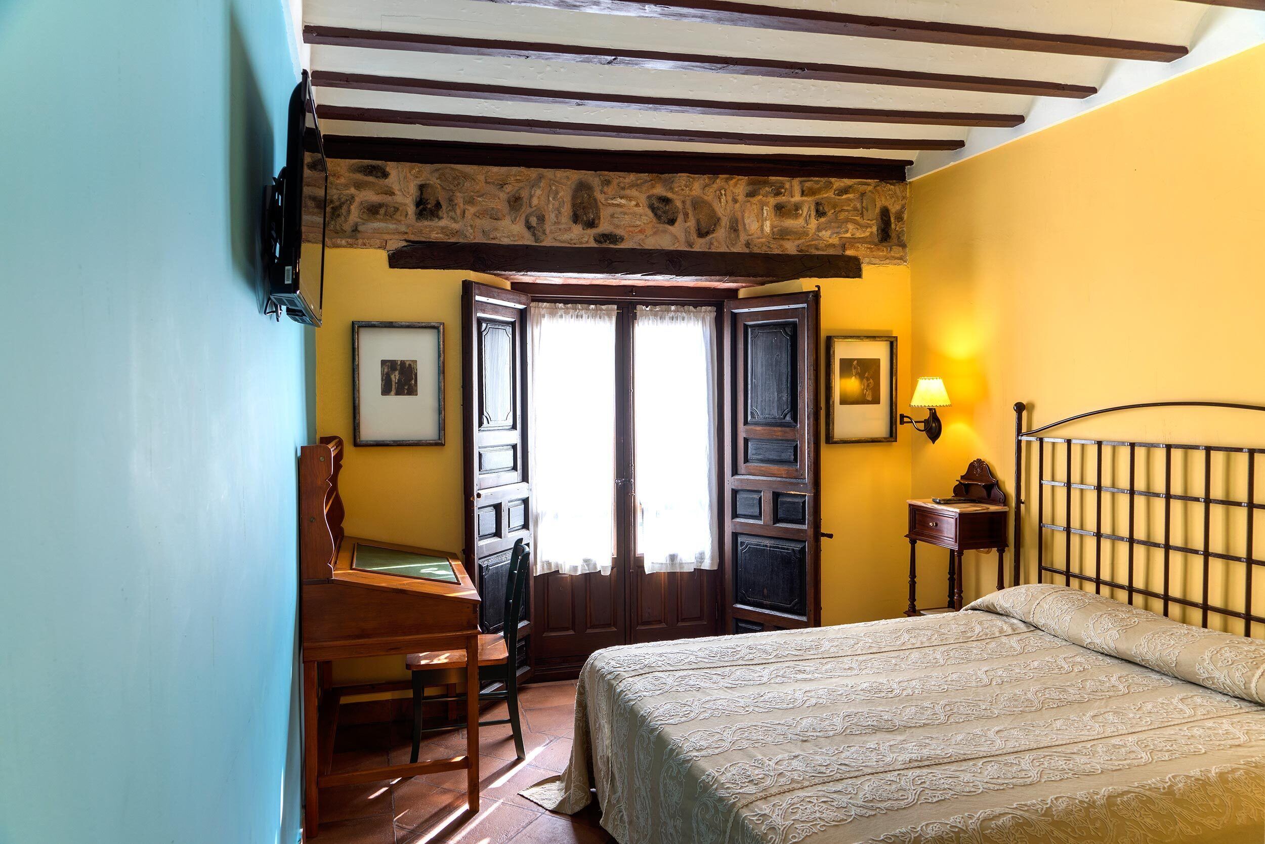 Quarto com cama, escrivaninha, cadeira e janela com cortinas.