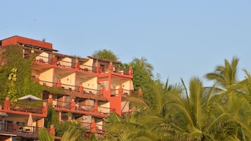 Um edifício com várias andares, varandas e um jardim tropical.