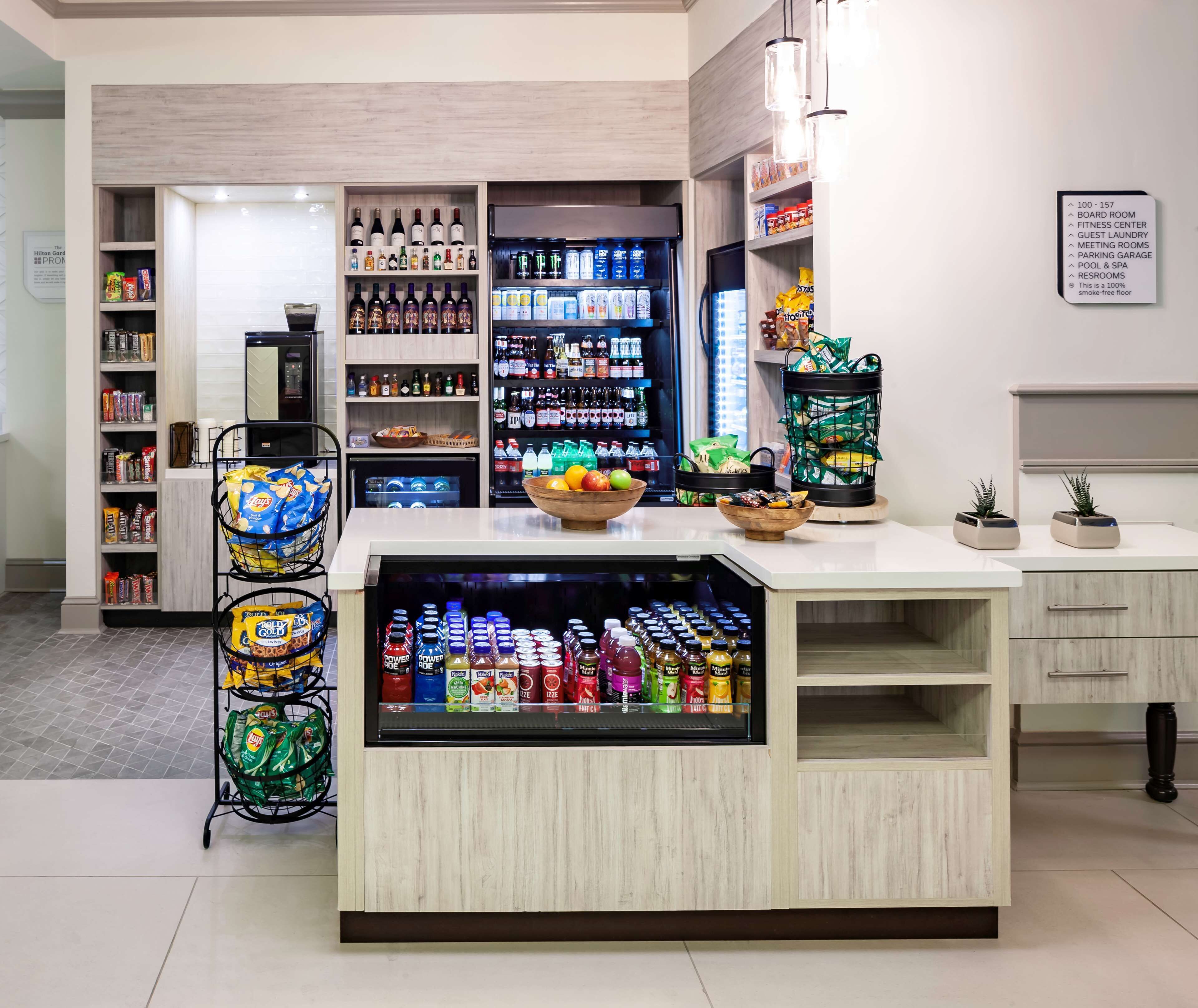 Um hall de hotel com um bar de lanches, diversas bebidas engarrafadas e um refrigerador de autoatendimento.