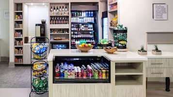 Um hall de hotel com um bar de lanches, diversas bebidas engarrafadas e um refrigerador de autoatendimento.