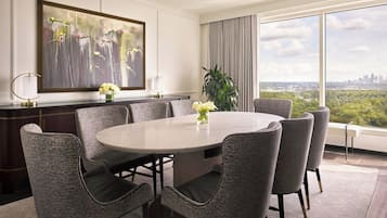 Uma sala de jantar moderna com uma mesa redonda, seis cadeiras, um quadro grande e vista para a cidade através de amplas janelas.