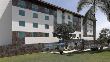 Um hotel de vários andares com fachada de pedra, várias janelas, área de estar ao ar livre com guarda-sóis e um gramado bem cuidado.
