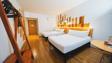 Quarto de hotel com duas camas de solteiro, piso de madeira, uma mesa redonda pequena e luminária fixada na parede.