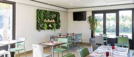 Uma sala de jantar moderna com cadeiras verdes, mesas de madeira e uma parede verde com um letreiro de neon.