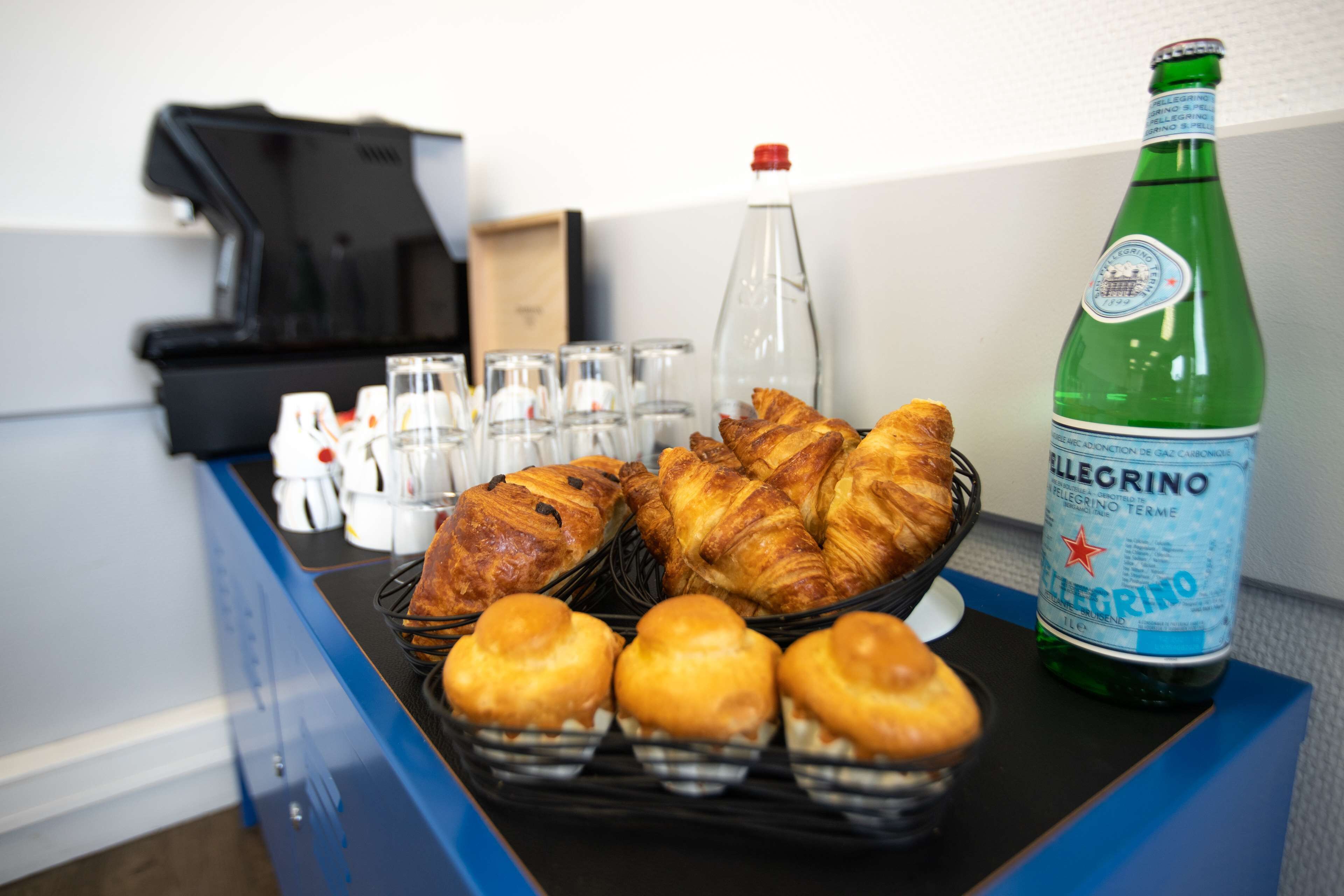 Um buffet de café da manhã com croissants, muffins e uma garrafa de água Pellegrino.