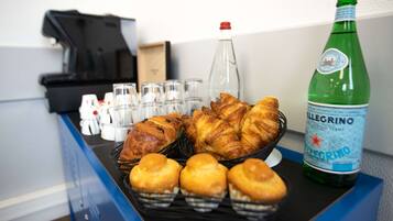 Um buffet de café da manhã com croissants, muffins e uma garrafa de água Pellegrino.