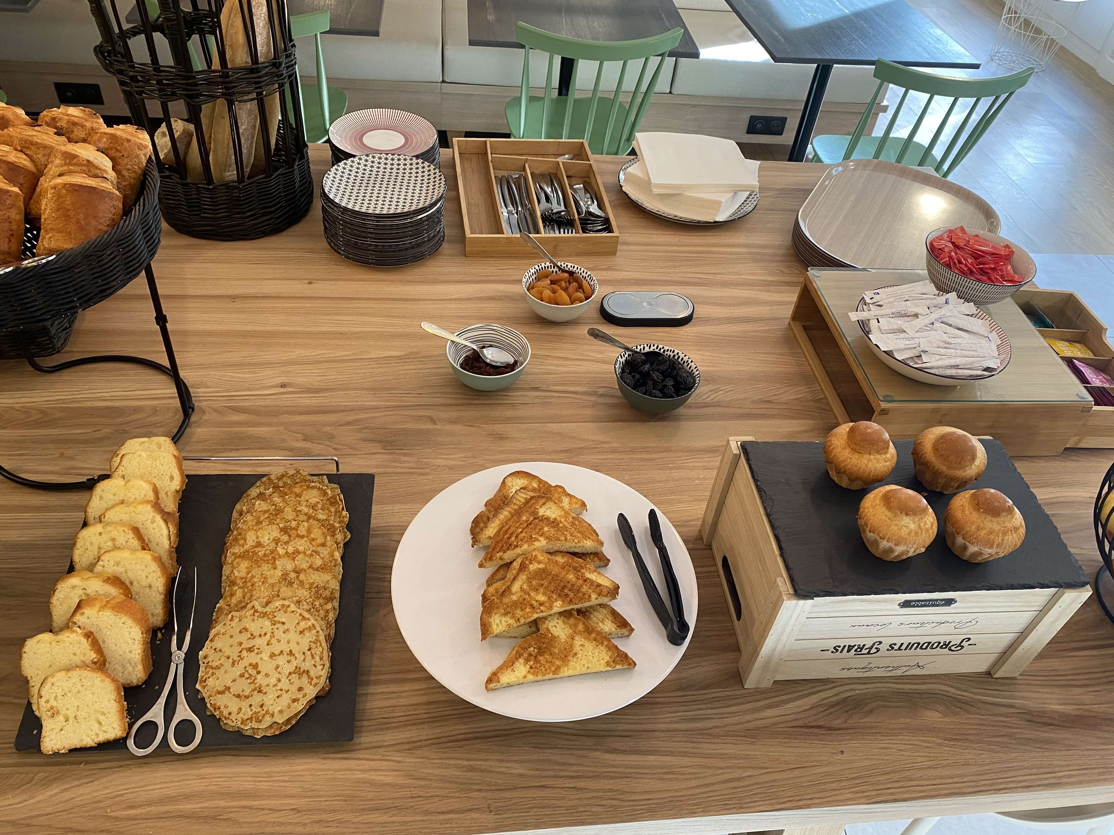 Buffet de café da manhã com diversos pães, doces e acompanhamentos.
