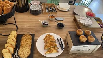 Buffet de café da manhã com diversos pães, doces e acompanhamentos.