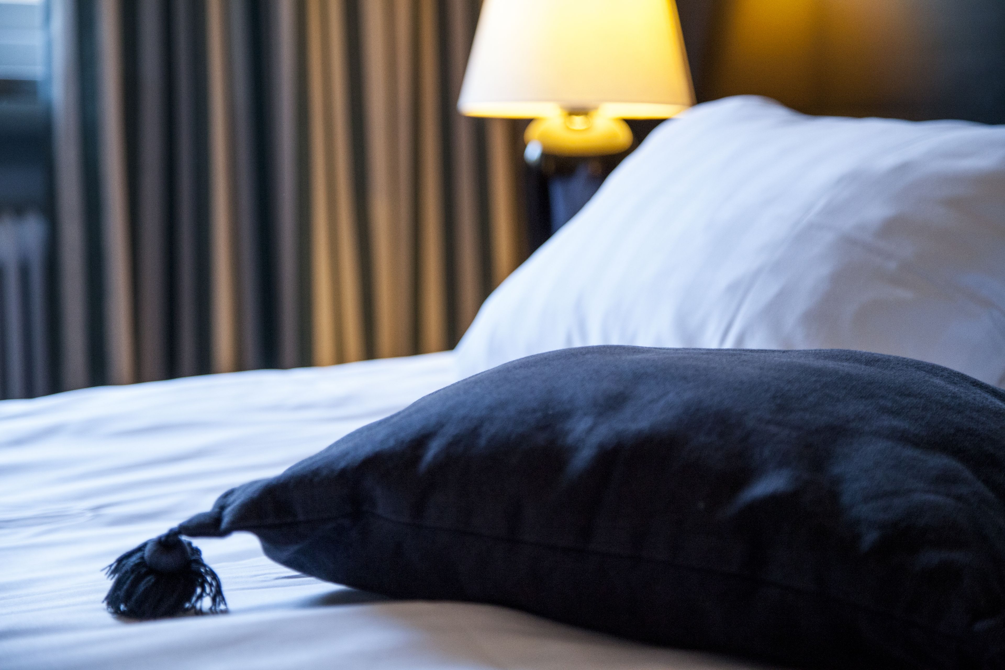 Uma cama com lençóis brancos e um travesseiro preto.