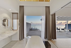 Casa de banho moderna com banheira, espelho redondo e vista para um terraço com área de estar ao ar livre.