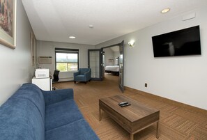Quarto de hotel com sofá azul, mesa de centro de madeira, televisão e cama com vista para o exterior.