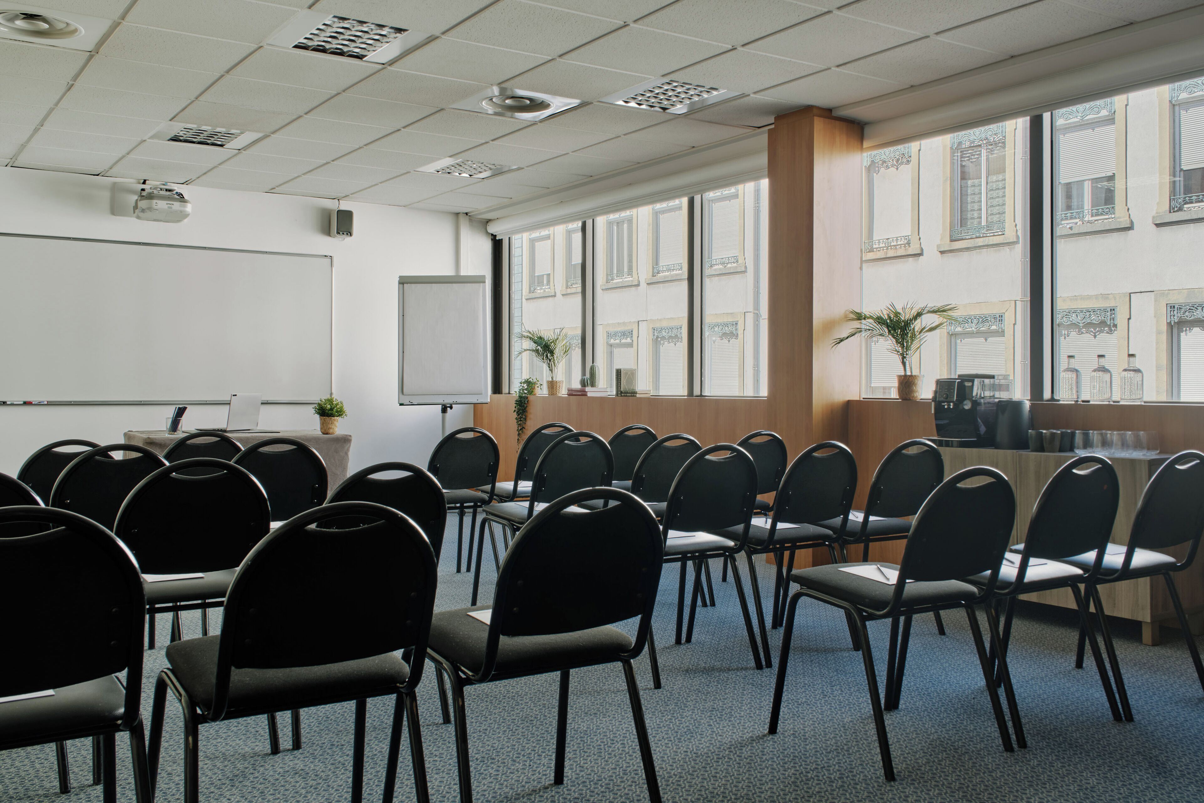 Sala de conferências com fileiras de cadeiras, um quadro branco e um projetor.