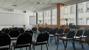 Sala de conferências com fileiras de cadeiras, um quadro branco e um projetor.