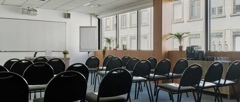 Sala de conferências com fileiras de cadeiras, um quadro branco e um projetor.