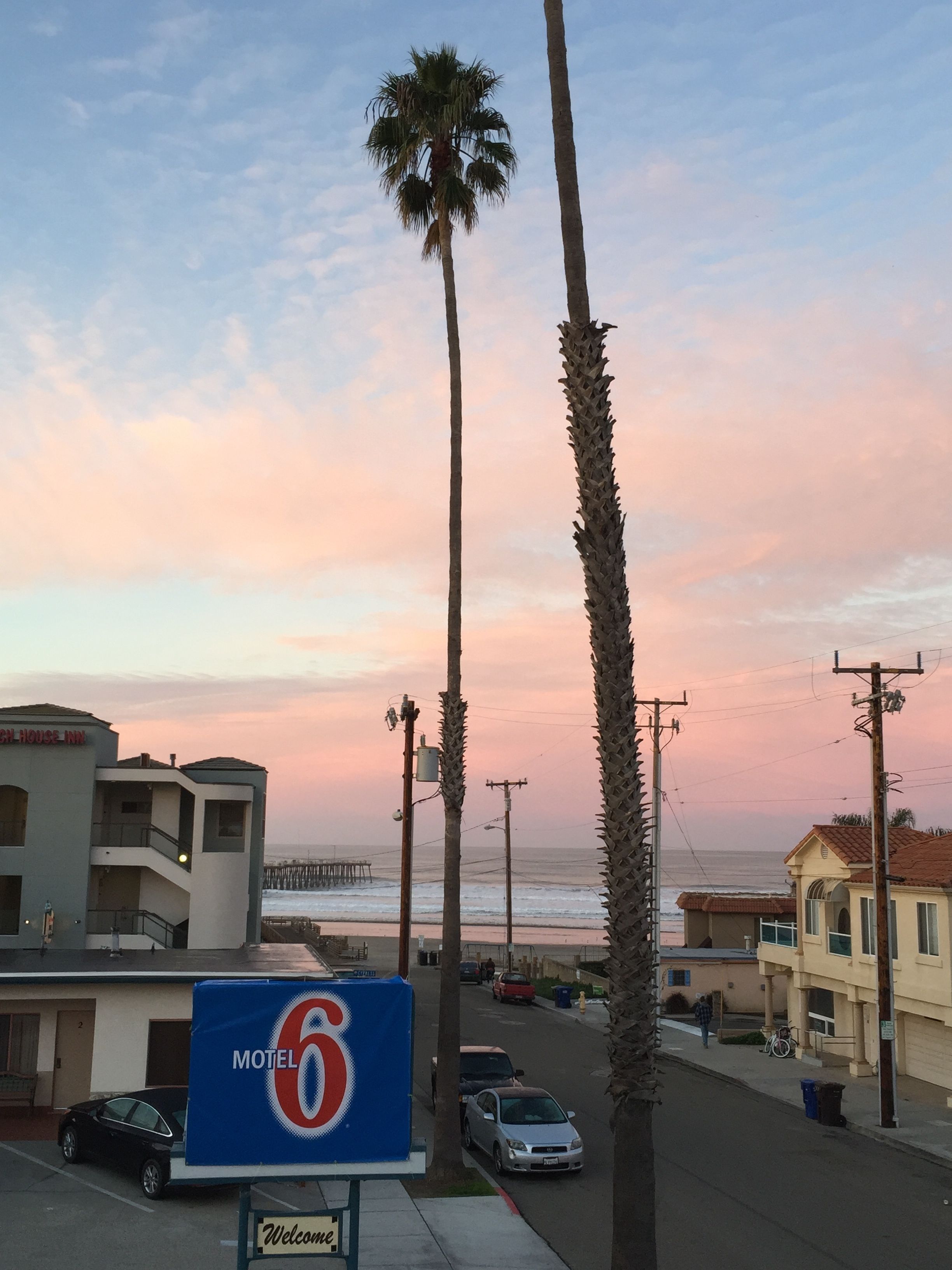 Um motel com vista para a praia, palmeiras e um céu ao pôr do sol.