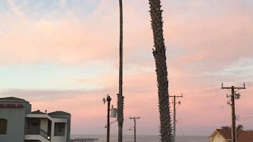 Um motel com vista para a praia, palmeiras e um céu ao pôr do sol.
