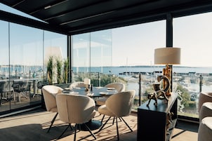 Espaço de jantar moderno com vista panorâmica para uma marina e paisagem urbana.