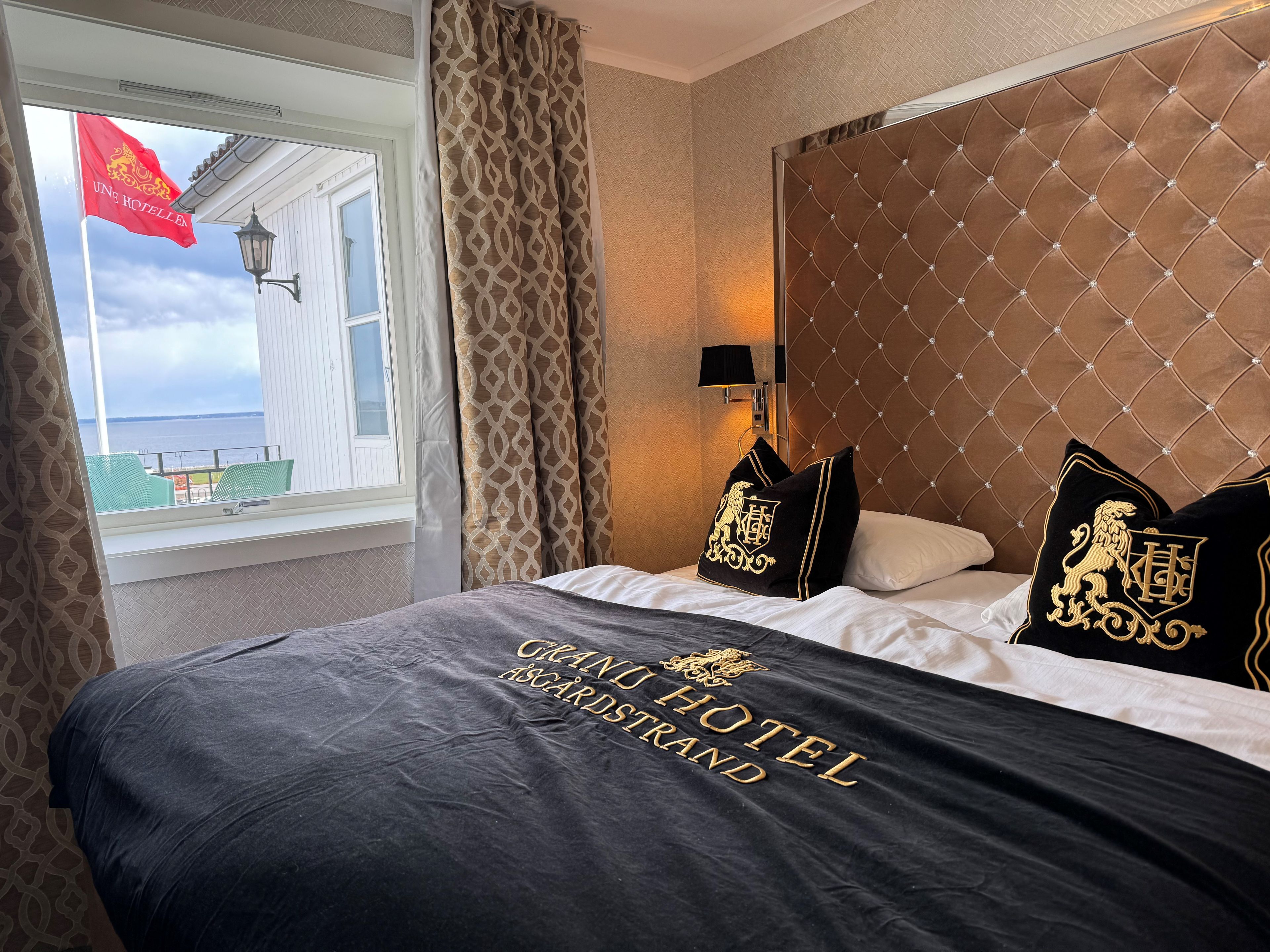 Quarto de hotel com uma cama grande, vista para o mar e uma bandeira.