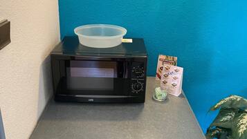 Uma área de cozinha com um micro-ondas em uma bancada, um recipiente de plástico e um pequeno cartão.