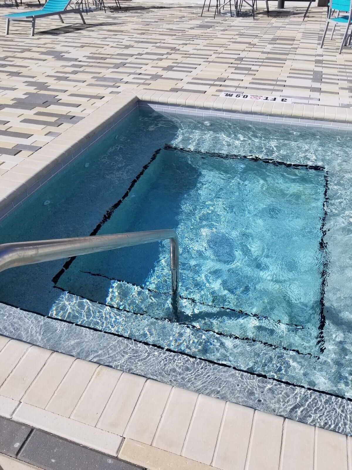 Piscina com linha de água cristalina, rodeada por um deck revestido de azulejos.