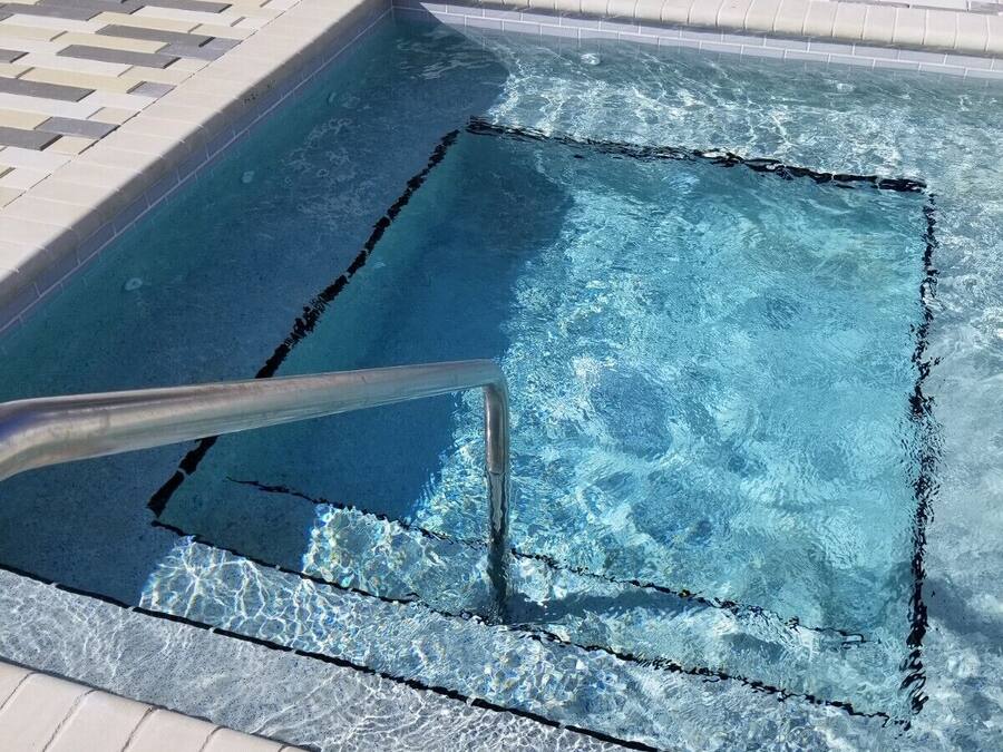 Piscina com linha de água cristalina, rodeada por um deck revestido de azulejos.