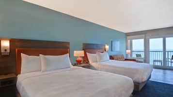 Quarto de hotel com duas camas, varanda com vista e um pequeno espaço para sentar.