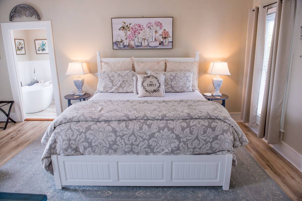 Quarto bem organizado com uma cama, duas mesas de cabeceira com luminárias, um espelho grande e um quadro na parede.