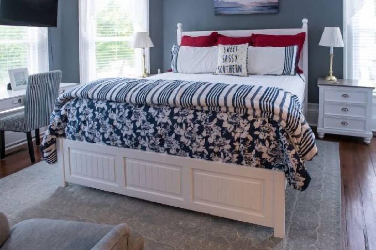 Quarto com cama, mesa de cabeceira, cadeira e janela.