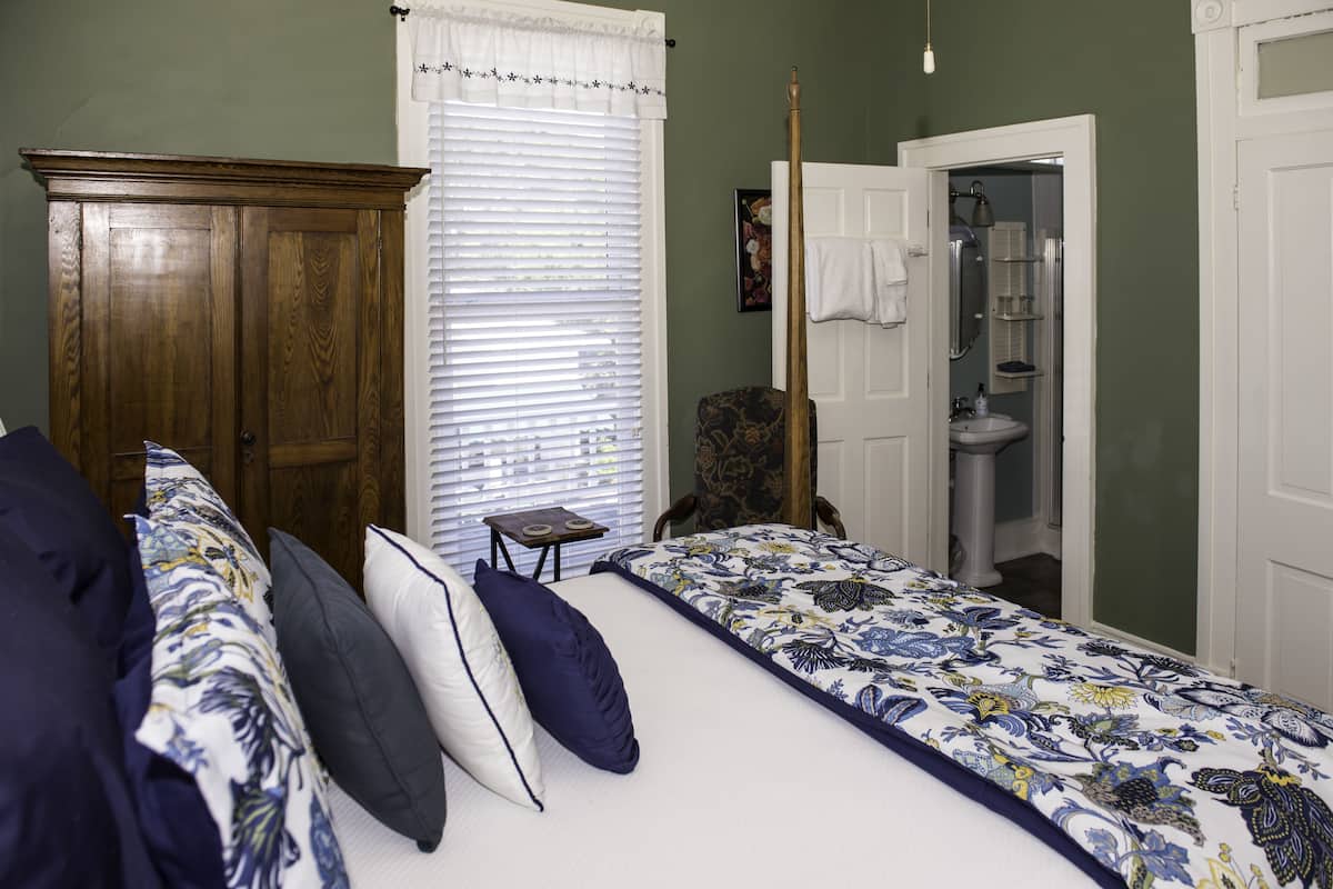 Quarto com cama, guarda-roupa de madeira, cadeira, mesa pequena e porta de banheiro.