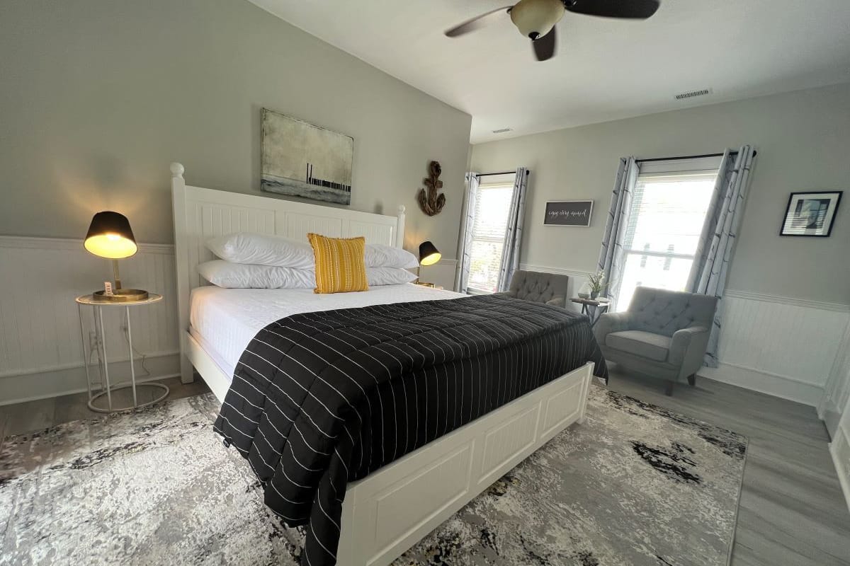 Quarto com cama grande, mesas de cabeceira, ventoinha no teto e janela com cortinas.