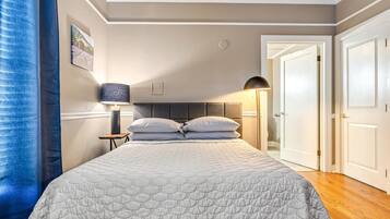 Quarto com cama, mesa de cabeceira, abajur e porta que dá para outro espaço.