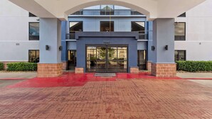Entrada de um edifício moderno com porta de vidro, o número 7887, e um caminho de tijolos vermelhos que leva até ele.
