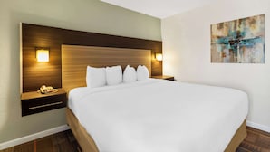 Quarto de hotel com cama grande, cabeceira de madeira, luminárias laterais e um quadro na parede.