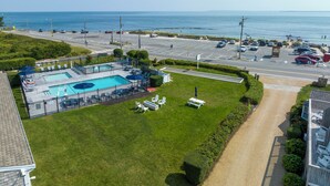 Uma área de piscina com várias piscinas e cadeiras de descanso, cercada por um gramado bem cuidado e um estacionamento cheio de carros.