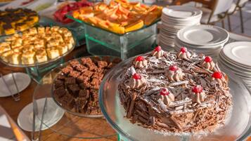 Uma mesa de buffet com diversos doces, incluindo um bolo de chocolate com chantilly e cerejas, e outras sobremesas variadas.