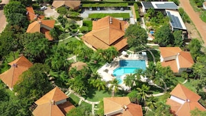 Vista aérea de um resort com vários edifícios, uma piscina central e vegetação ao redor.
