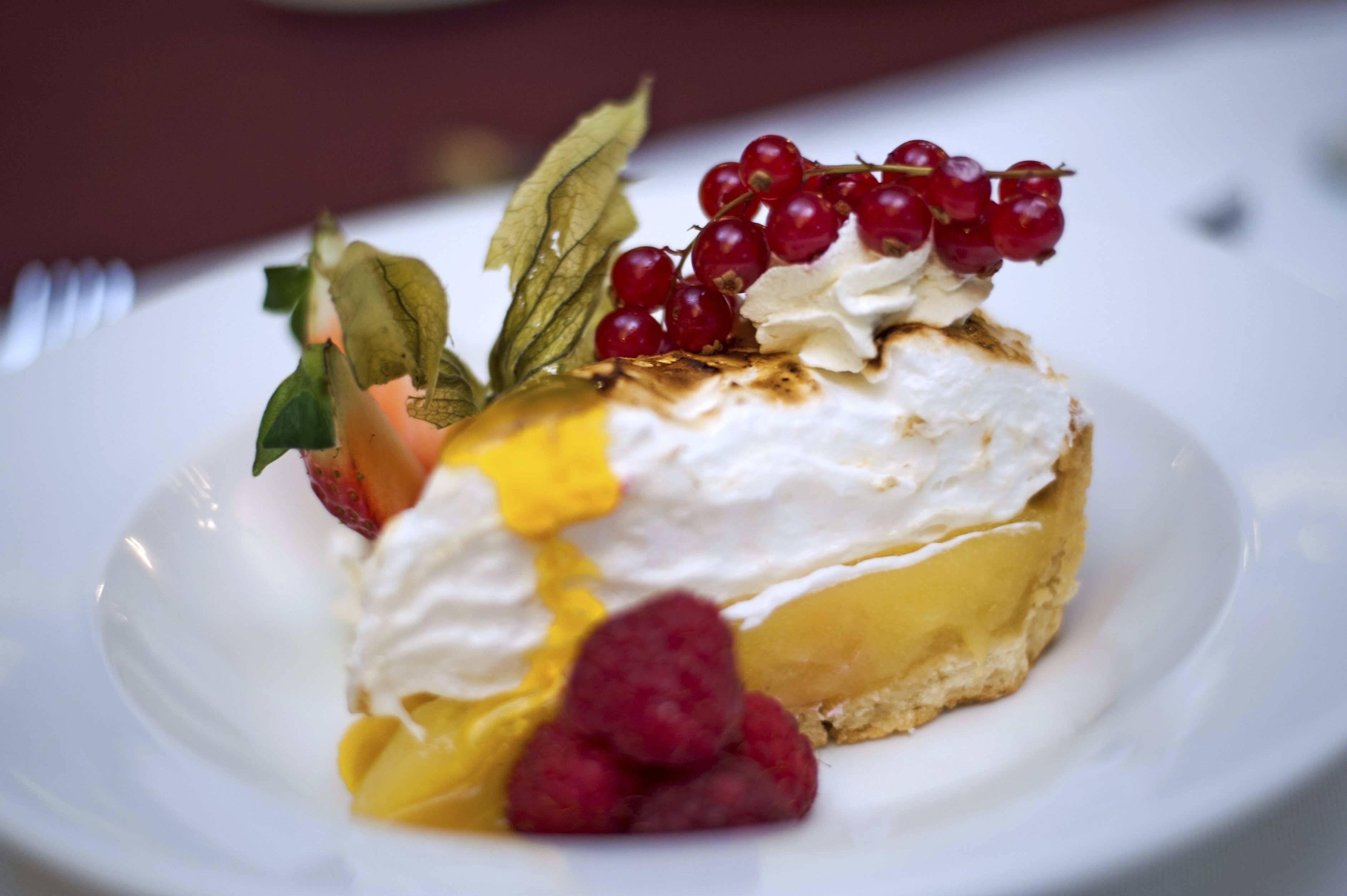 Sobremesa com chantilly, frutos vermelhos e uma fatia de bolo sobre um prato branco.