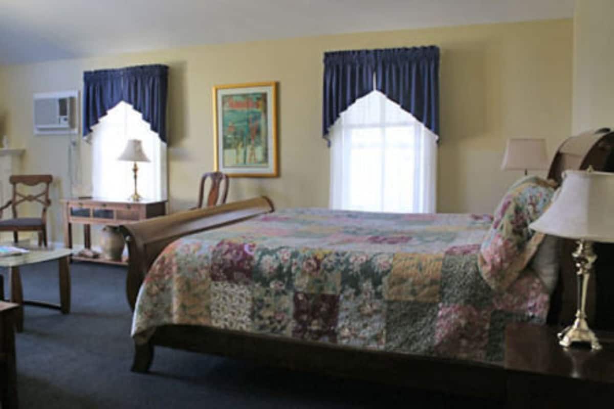 Quarto com cama, escrivaninha, cadeira e janela com cortinas.