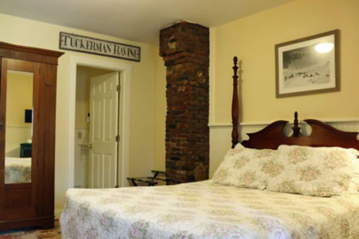 Quarto com cama, armário de madeira, parede de tijolos e porta com a inscrição "TUCKERMAN RAVINE".