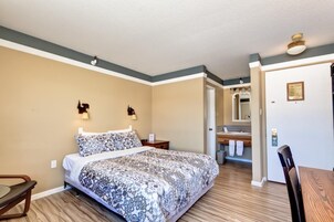 Quarto com cama, mesas de cabeceira, uma cadeira, escrivaninha e banheiro com pia e espelho.