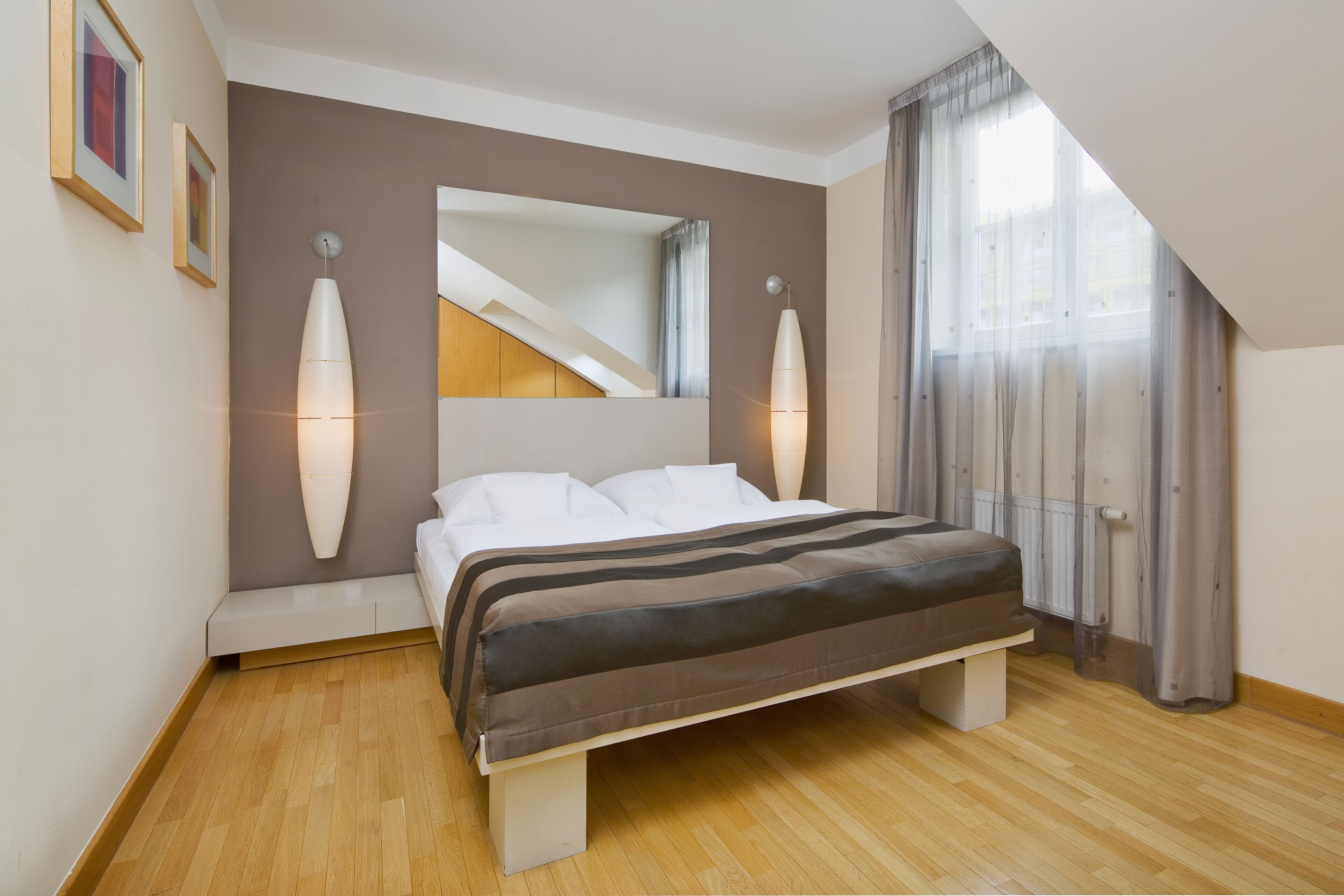 Quarto com cama, piso de madeira, teto inclinado e janela com cortinas.