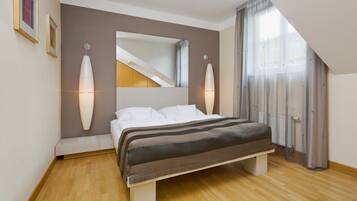 Quarto com cama, piso de madeira, teto inclinado e janela com cortinas.