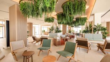 Um hall amplo com móveis modernos, plantas pendentes e uma área de estar central.
