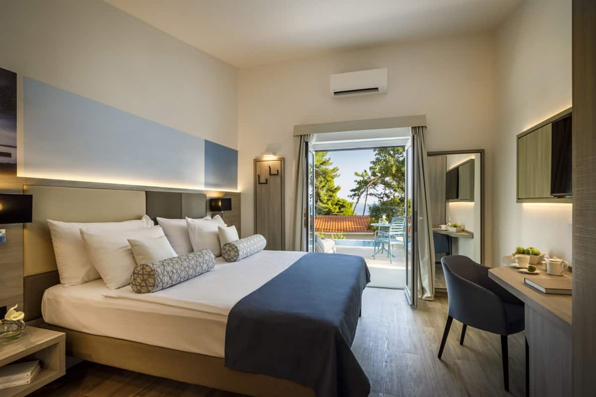 Quarto de hotel moderno com uma cama grande, uma escrivaninha e vista para o exterior.